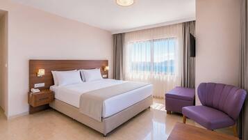 Quarto de hotel com uma cama grande, mesa de cabeceira, uma cadeira, televisão de tela plana e vista para o exterior.