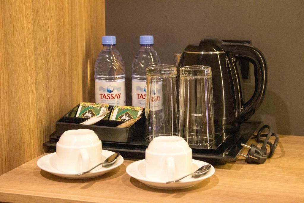 Uma mesa de café da manhã com duas xícaras, duas garrafas de água, uma cafeteira e uma bandeja com sachês de chá e uma colher.