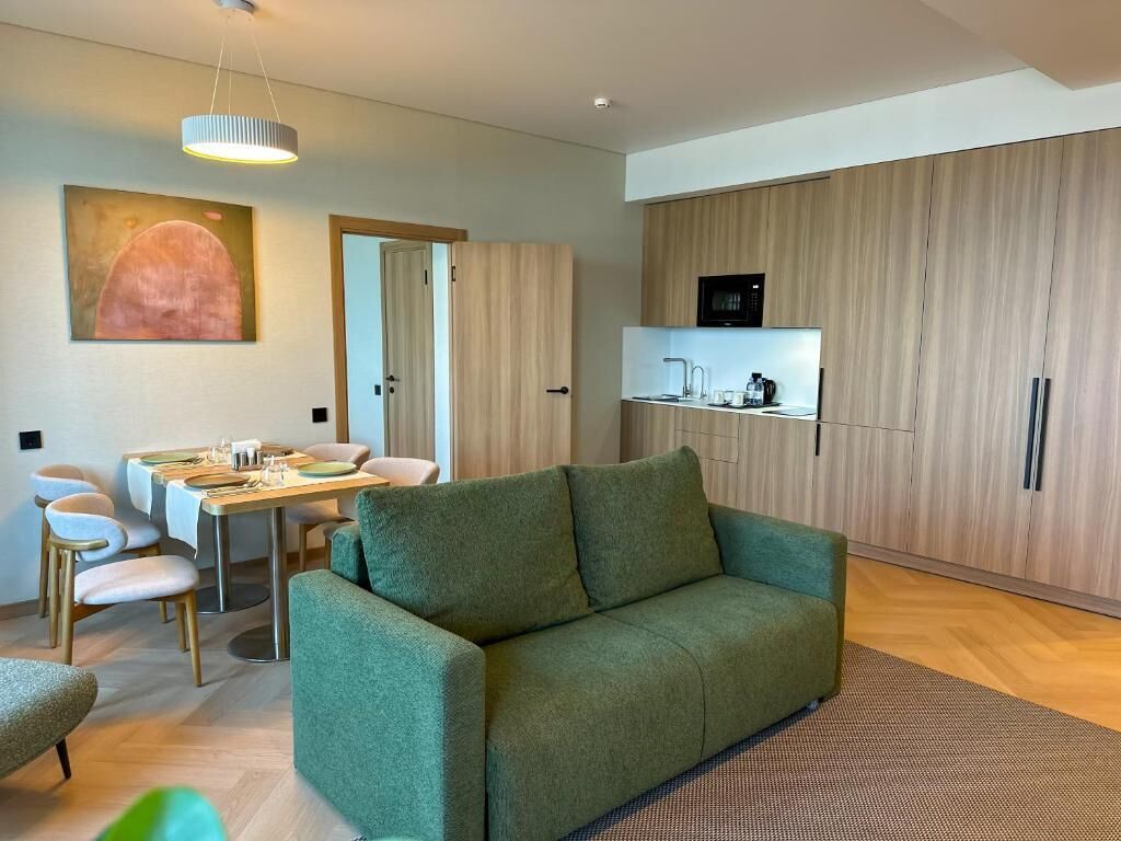 Uma sala de estar moderna com sofá, mesa de jantar, cadeiras e uma cozinha com armários e micro-ondas.