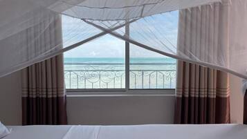 Um quarto com cama, janela com cortinas e vista para o oceano.