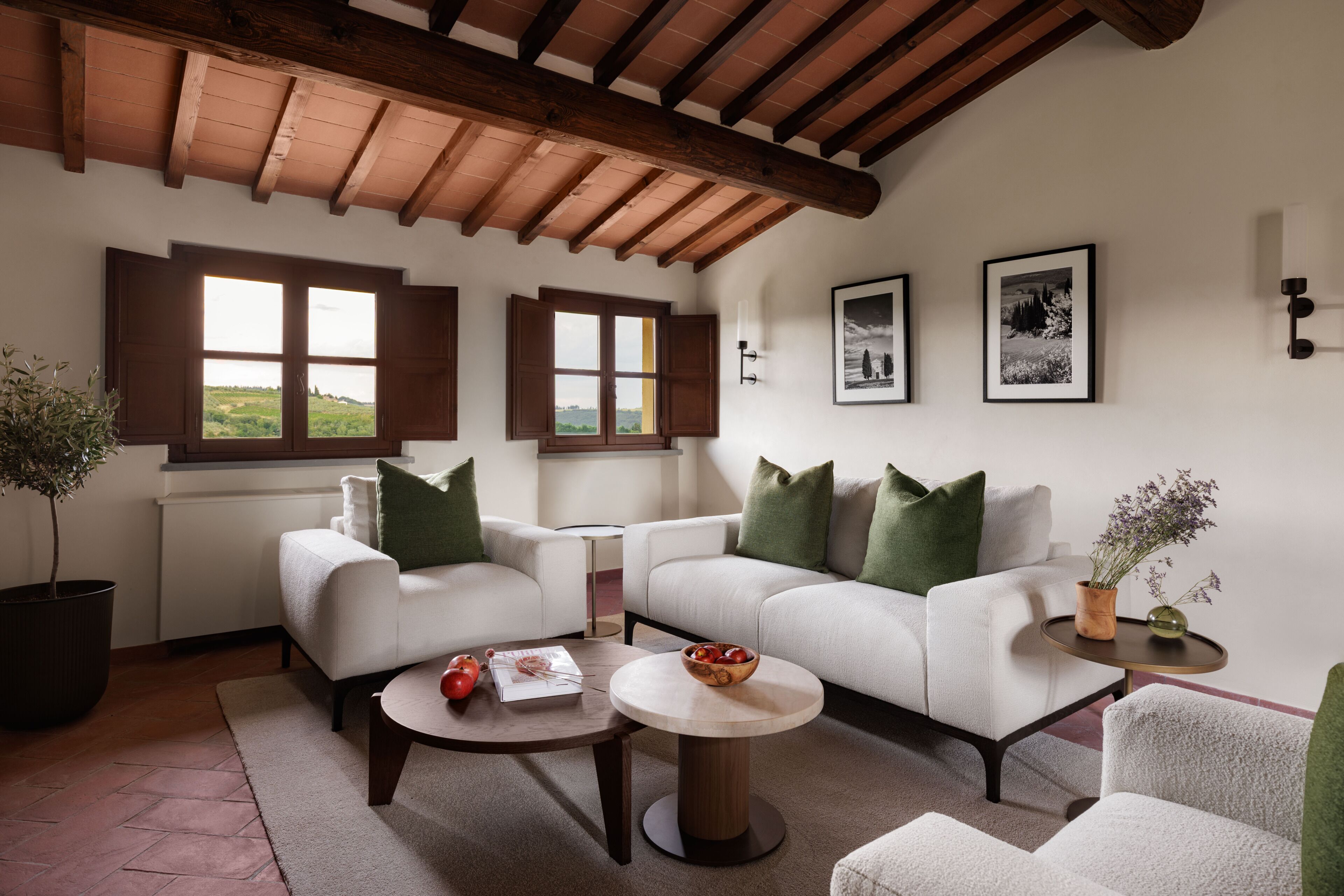 Uma sala de estar com um sofá branco, duas mesinhas de centro redondas, uma planta em vaso e vista através de grandes janelas.