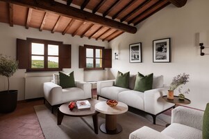 Uma sala de estar com um sofá branco, duas mesinhas de centro redondas, uma planta em vaso e vista através de grandes janelas.