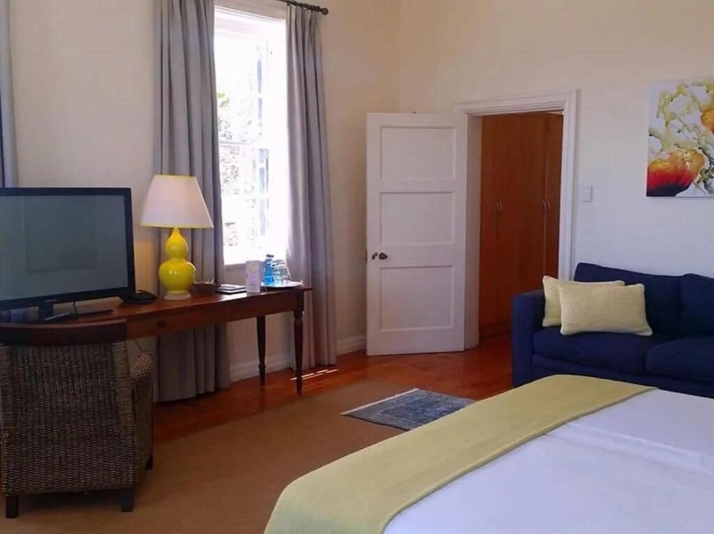 Quarto de hotel com cama, televisão, escrivaninha com abajur, sofá azul e porta.