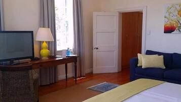 Quarto de hotel com cama, televisão, escrivaninha com abajur, sofá azul e porta.