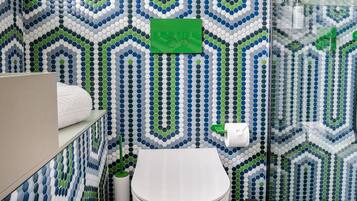 Casa de banho com sanita branca, dispensador de sabonete verde e parede com azulejos estampados.