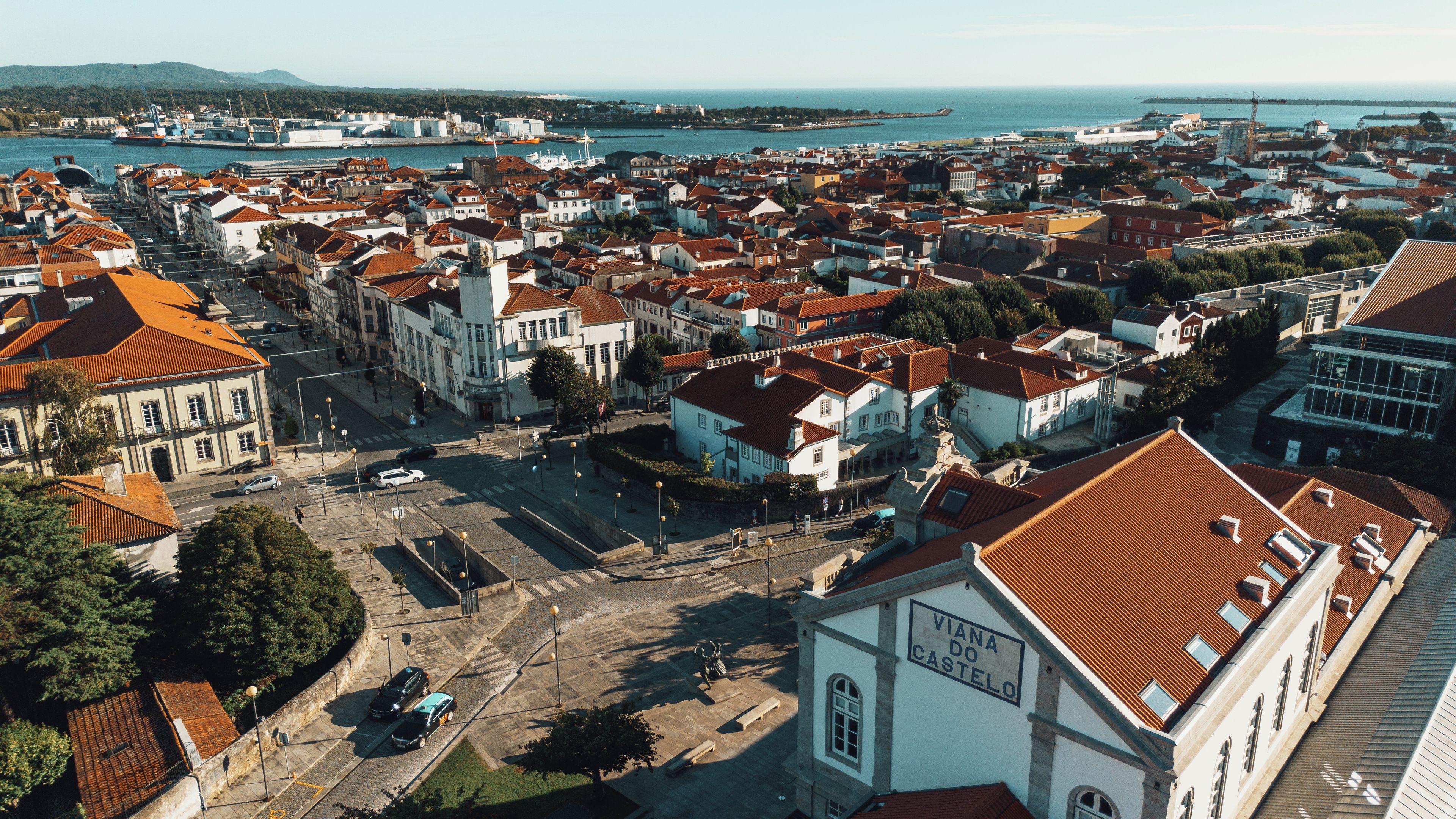 Uma vila costeira com edifícios históricos, uma praça central e vista para o mar.