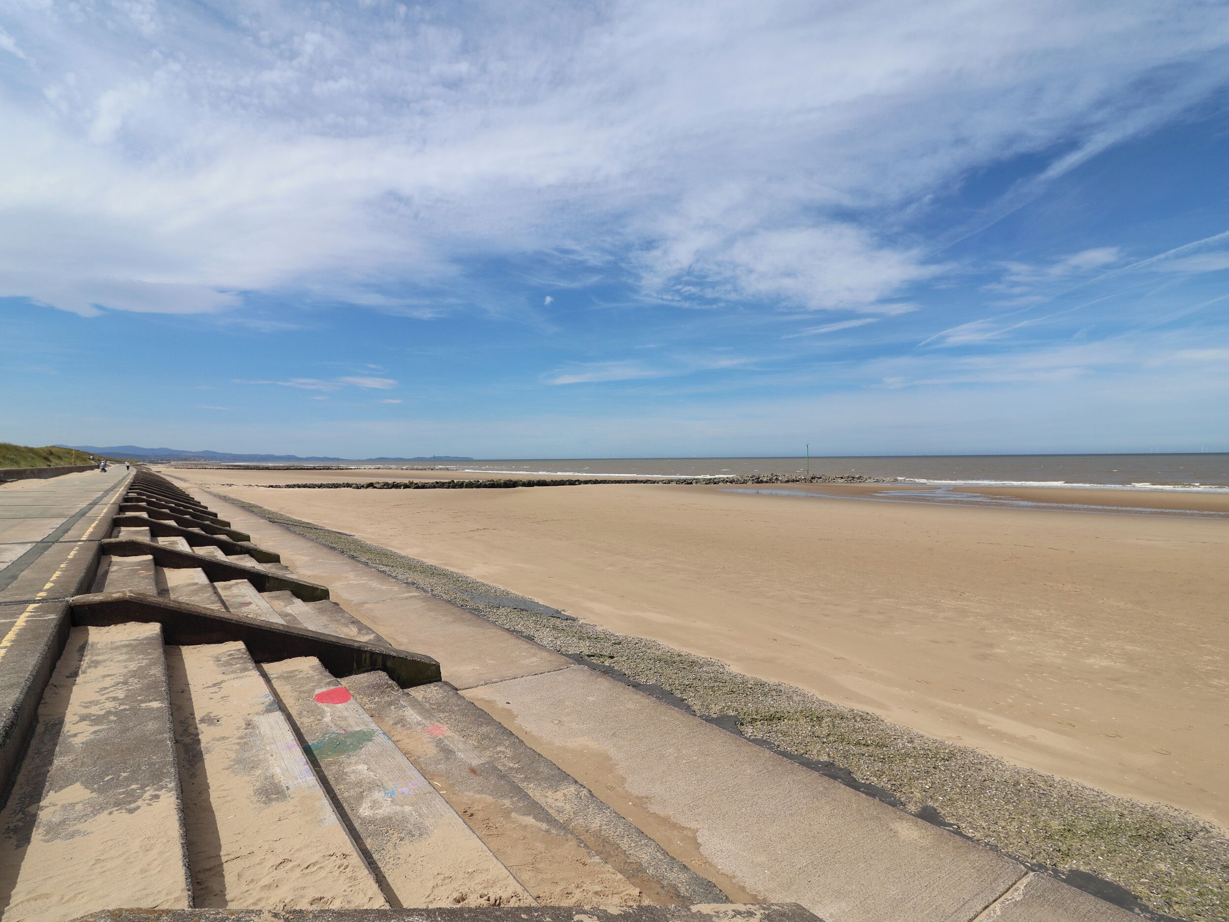Uma praia com um calçadão de concreto e um molhe rochoso.
