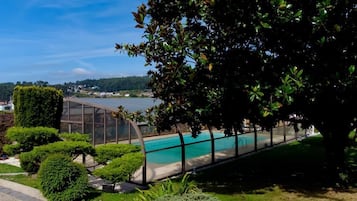 Piscina com vista para um corpo d'água, rodeada por vegetação bem cuidada e céu claro.