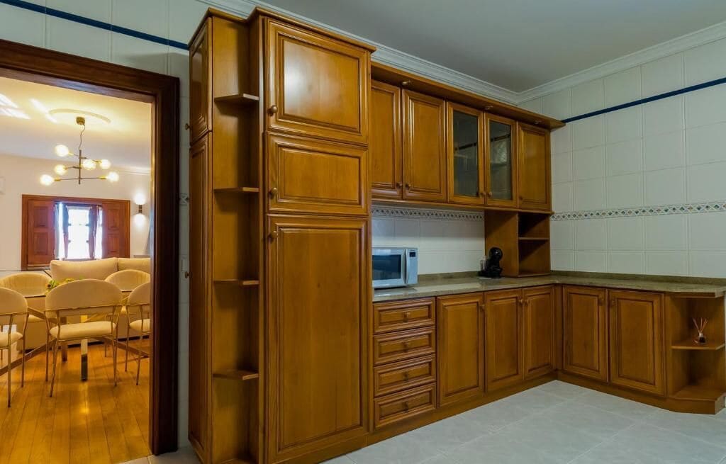 Uma cozinha com armários de madeira, micro-ondas e um espaço de refeições com cadeiras.