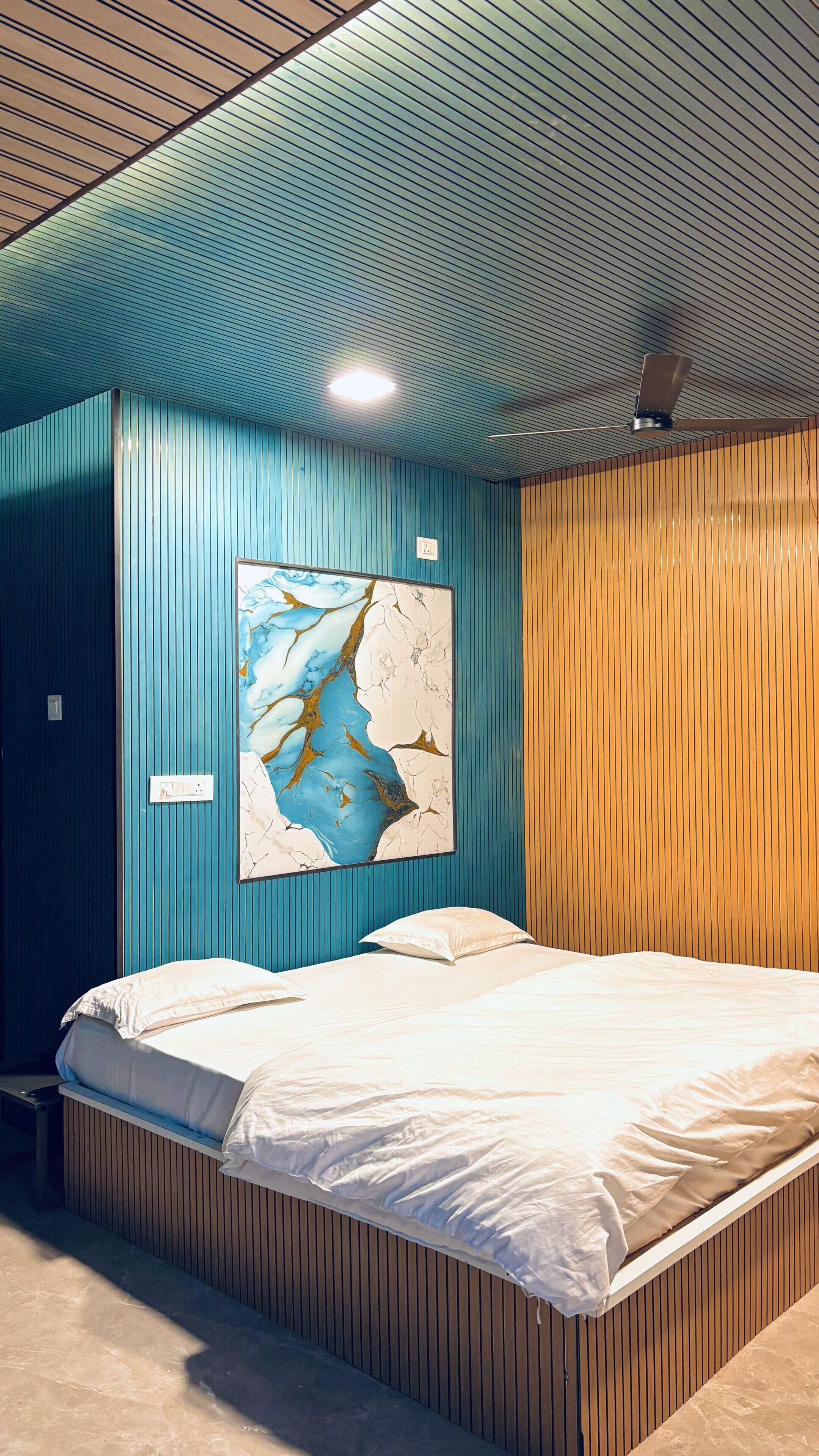 Quarto moderno com cama, ventoinha no teto e quadro na parede.