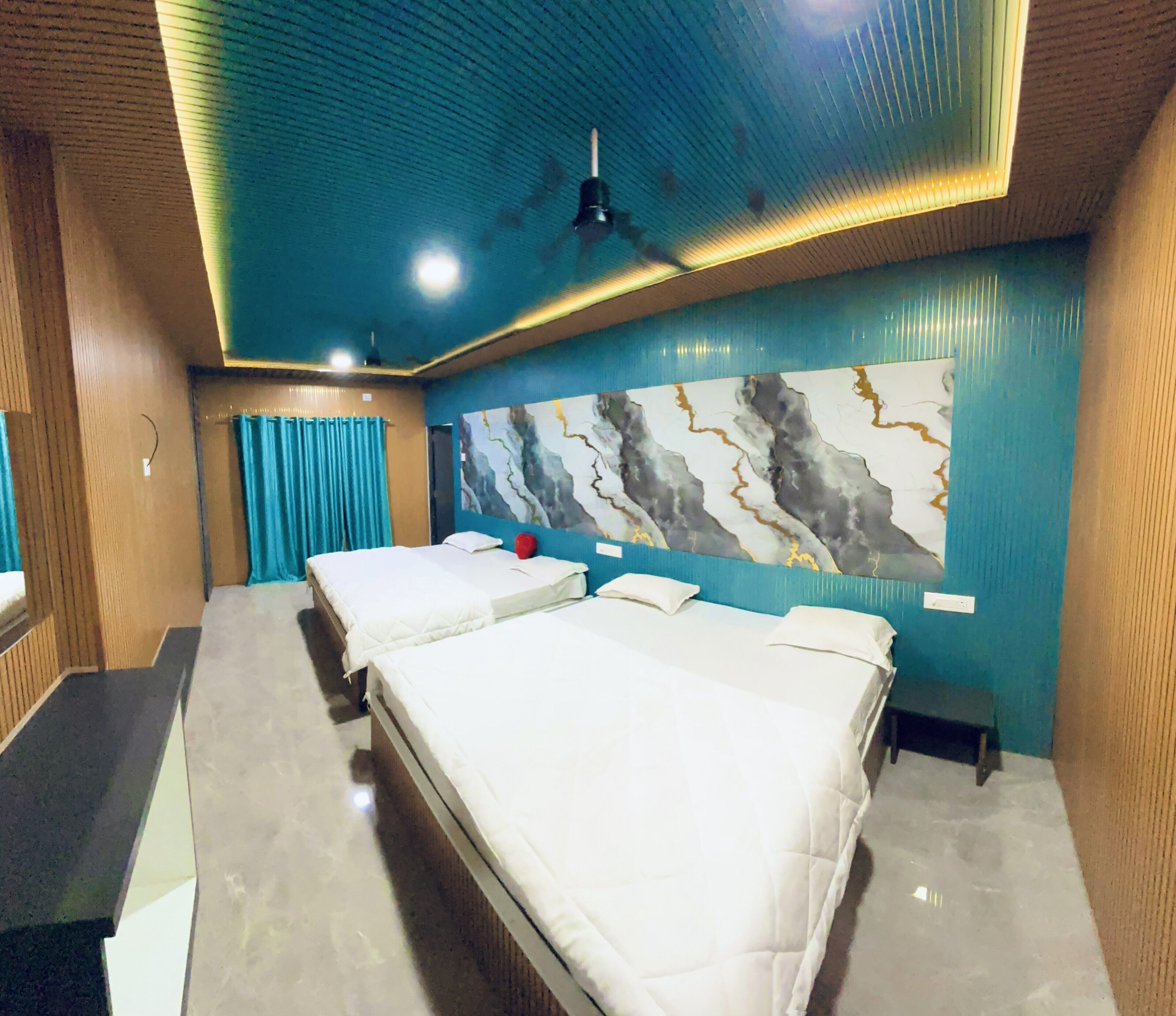Quarto de hotel com duas camas, um ventilador de teto e uma grande pintura abstrata na parede.