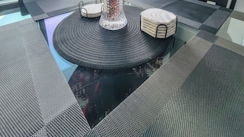 Uma sala de jantar moderna com mesa de vidro, jogos americanos trançados pretos e um vaso decorativo com flores vermelhas e amarelas.