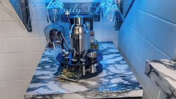 Uma cozinha com bancada de mármore, armário preto e luminária neon.