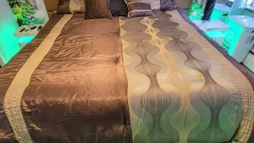 Uma cama com colcha estampada, várias almofadas, uma cabeceira e uma mesa de cabeceira com abajur.