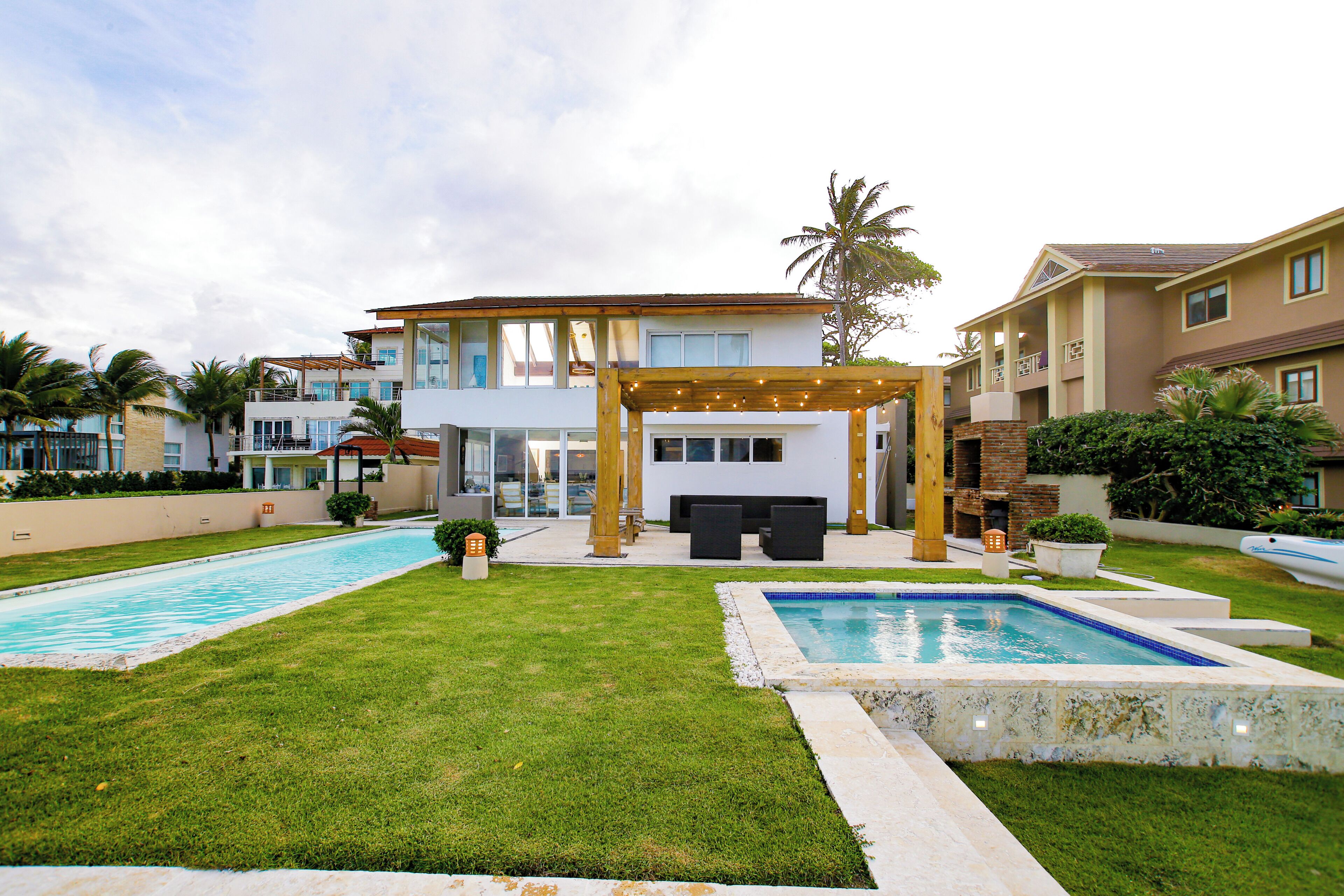 Uma casa moderna com duas piscinas, um terraço coberto e um gramado bem cuidado.