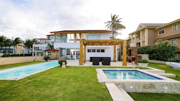 Uma casa moderna com duas piscinas, um terraço coberto e um gramado bem cuidado.