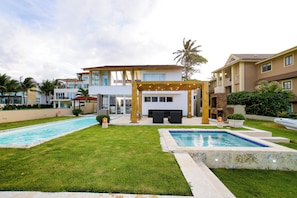 Uma casa moderna com duas piscinas, um terraço coberto e um gramado bem cuidado.