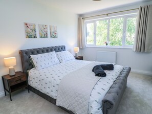 Quarto com cama, mesas de cabeceira, janela com cortinas e obras de arte na parede.