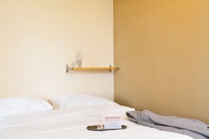 Quarto de hotel com uma cama, uma mesinha de cabeceira com um tabuleiro contendo um copo de água, uma garrafa pequena e um cartão.