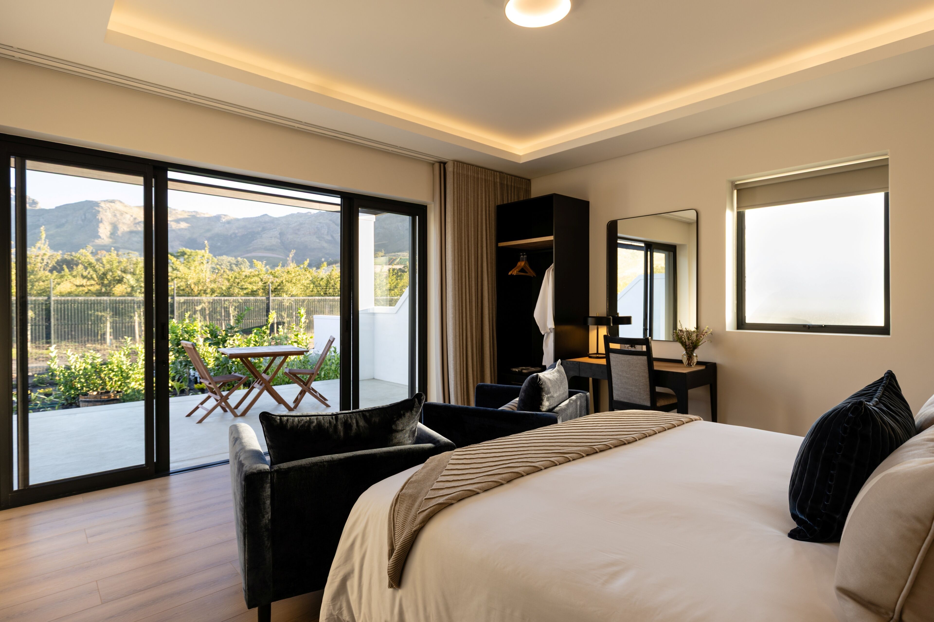 Quarto de hotel com uma cama grande, uma escrivaninha, uma cadeira e varanda com vista para as montanhas.