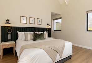 Quarto com cama, mesas de cabeceira, um criado-mudo, janela e obra de arte na parede.
