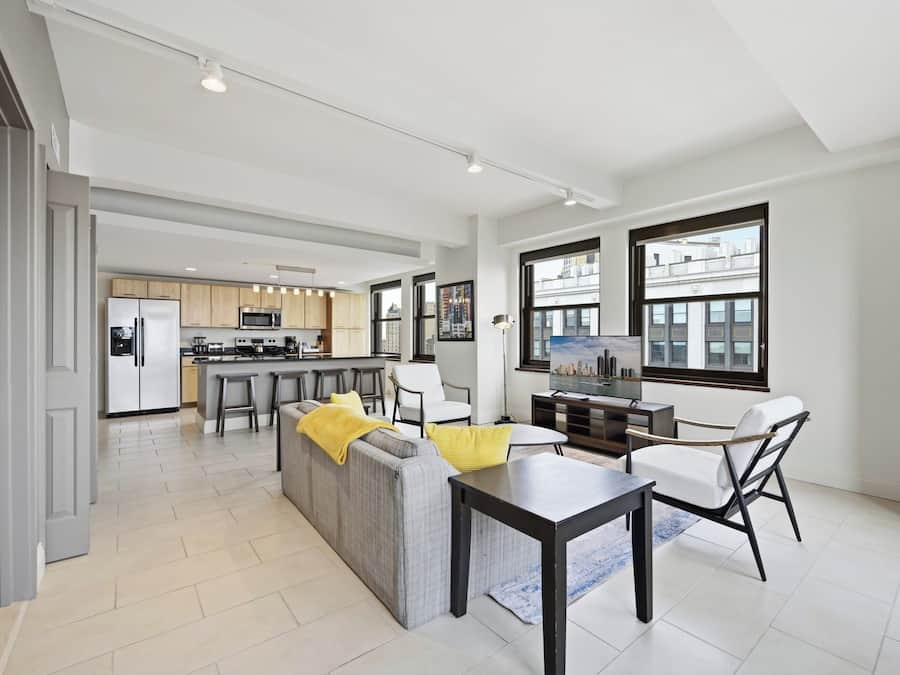 Uma cozinha moderna com uma ilha central, sala de jantar com mesa e cadeiras, e sala de estar com sofá e televisão.