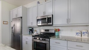 Cozinha moderna com eletrodomésticos de aço inoxidável, armários brancos e bancada de granito.