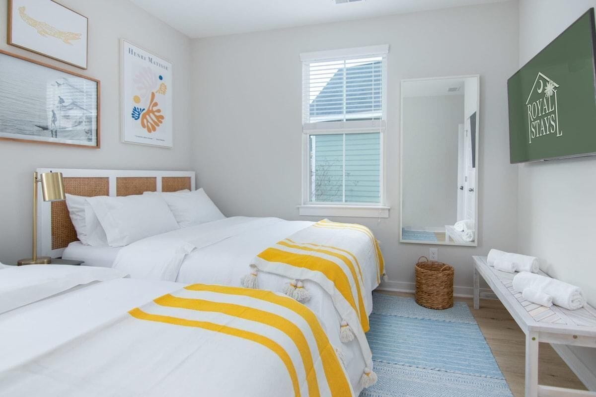 Quarto de hotel com duas camas, um espelho grande, uma cesta de vime e um banco com toalhas.
