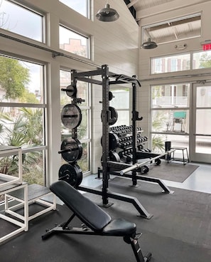 Uma academia com equipamentos de musculação, bancos e amplas janelas com vista para o exterior.