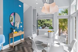 Uma sala de jantar moderna com uma mesa redonda, cadeiras brancas e uma parede azul decorativa.