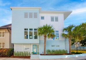 Uma casa moderna de dois andares com porta azul, revestimento branco e o número '4499' na fachada.