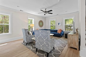 Uma sala de estar espaçosa com um sofá azul, poltronas estampadas e um ventilador de teto.