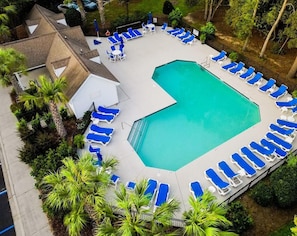 Vista aérea de uma piscina com cadeiras de descanso azuis dispostas ao redor, cercada por vegetação e uma área cercada.