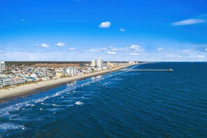 Paisagem costeira com praia, oceano e um píer que se estende sobre a água.