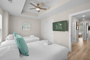 Quarto de hotel com duas camas, um ventilador de teto, um quadro e uma placa com a inscrição 'ROYAL STAYS'.