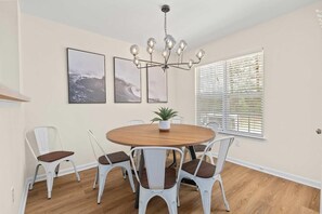 Uma sala de jantar com uma mesa de madeira redonda, cadeiras brancas, um candelabro e quadros nas paredes.