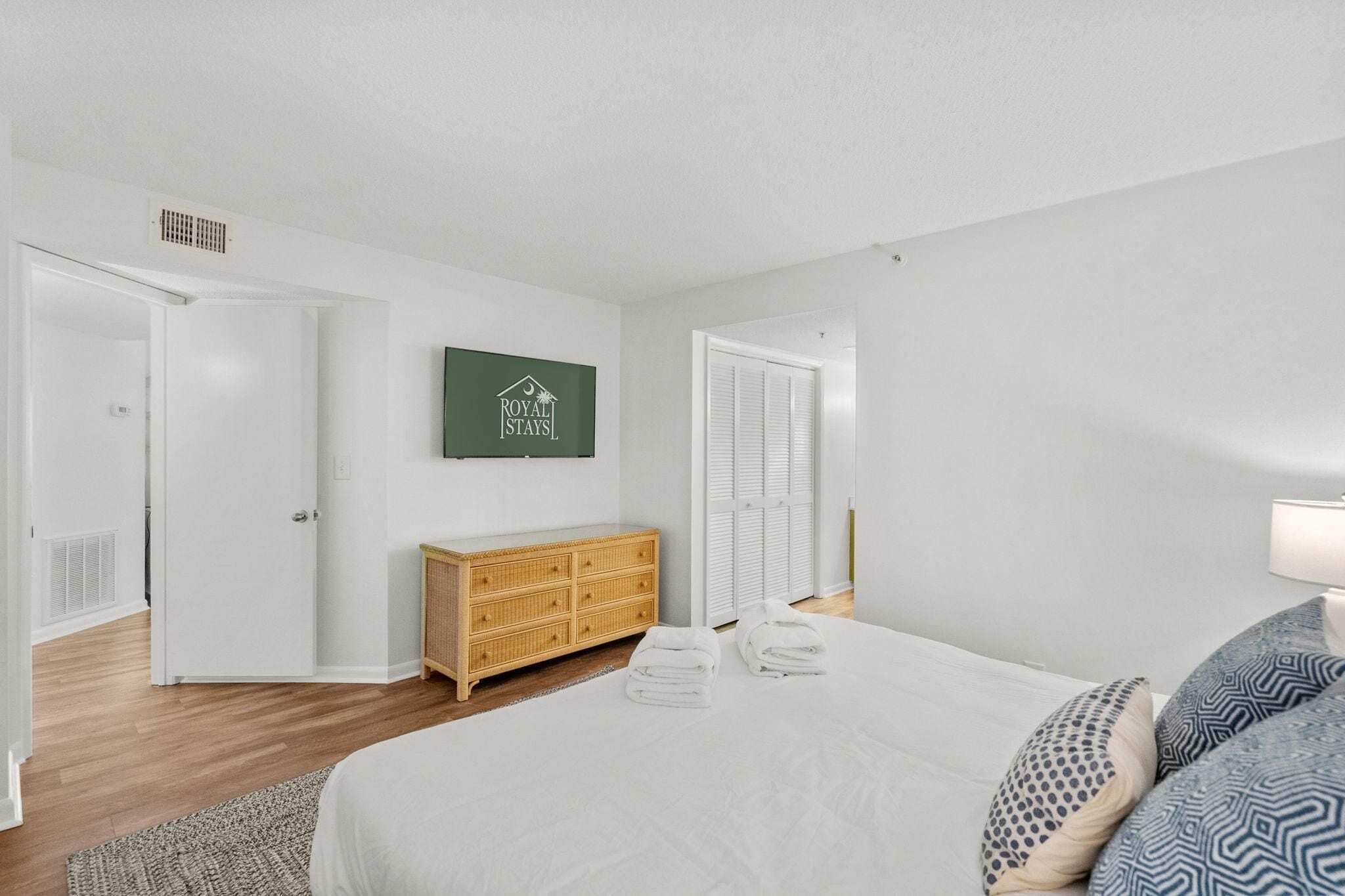 Quarto de hotel com cama, cómoda de madeira, placa na parede e porta que dá para outro quarto.