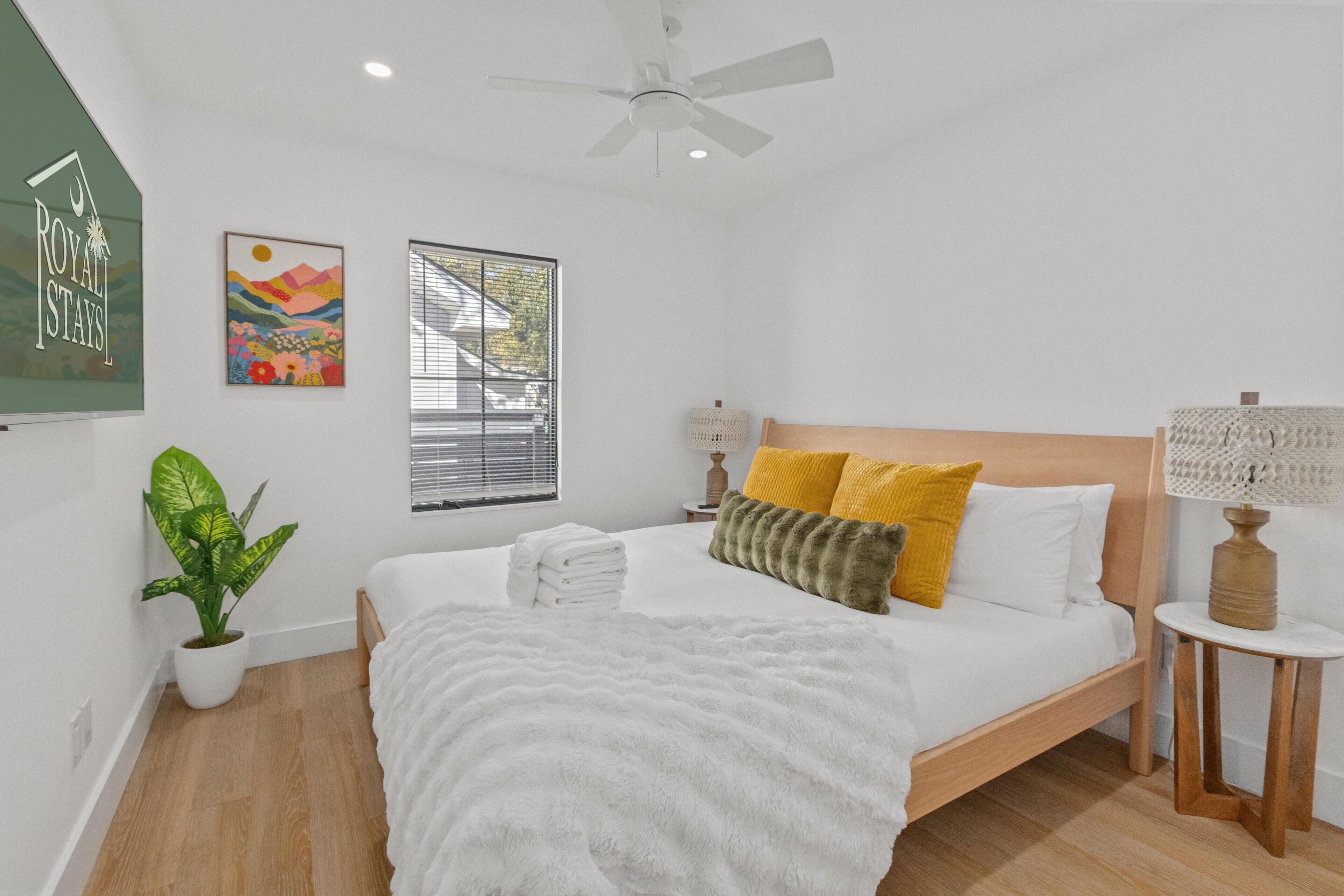 Quarto moderno com cama, ventoinha no teto, janela e planta em vaso.