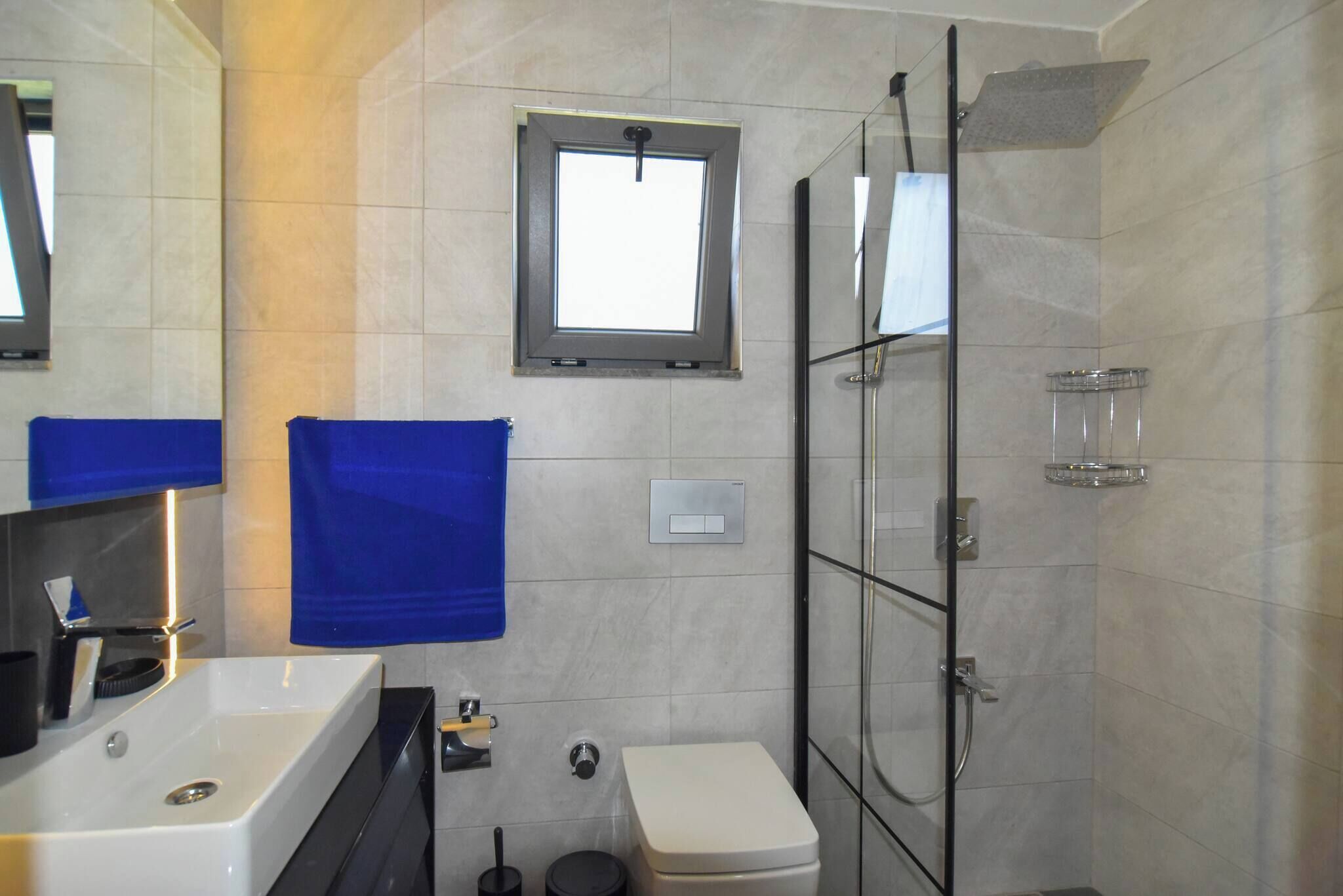 Casa de banho moderna com cabine de chuveiro em vidro, sanita branca e toalha azul pendurada na parede.