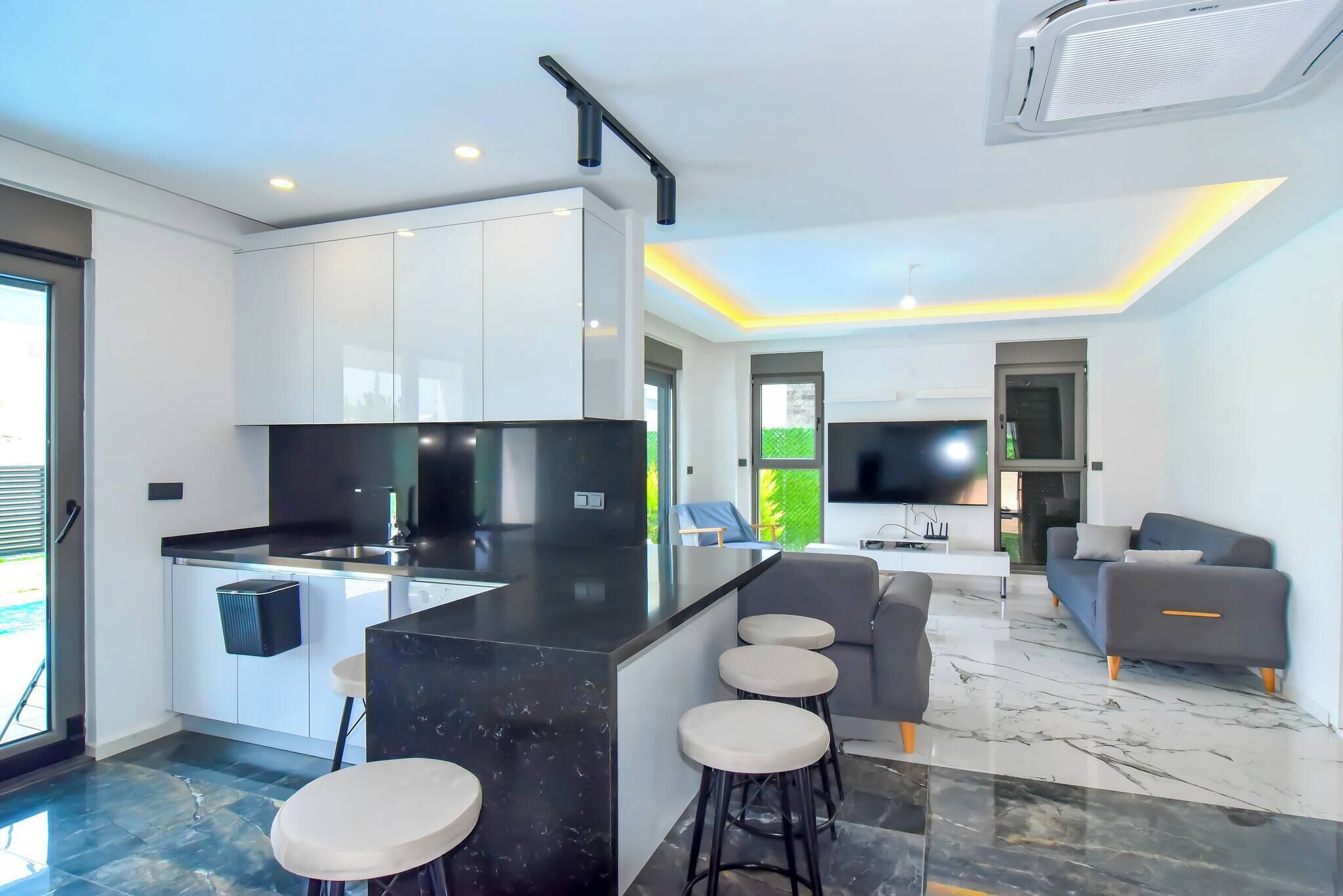 Uma cozinha moderna com ilha central, banquetas e área de jantar com sofá e televisão.