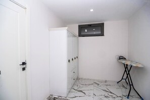 Um quarto pequeno com um armário branco, uma janela e um centro de passar roupa portátil.