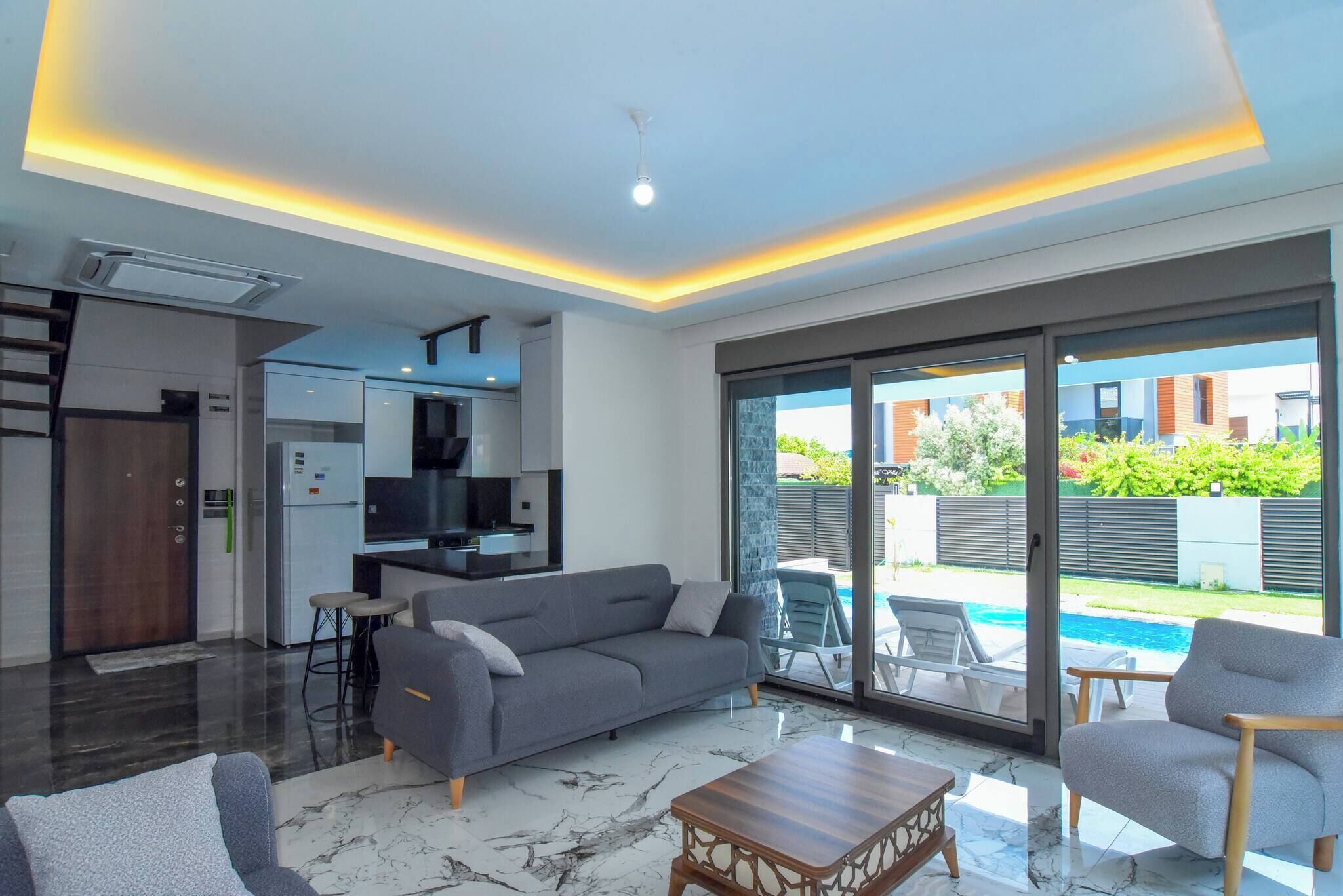 Uma sala de estar moderna com um sofá, mesa de centro e vista para uma piscina através de amplas portas de correr.