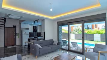 Uma sala de estar moderna com um sofá, mesa de centro e vista para uma piscina através de amplas portas de correr.
