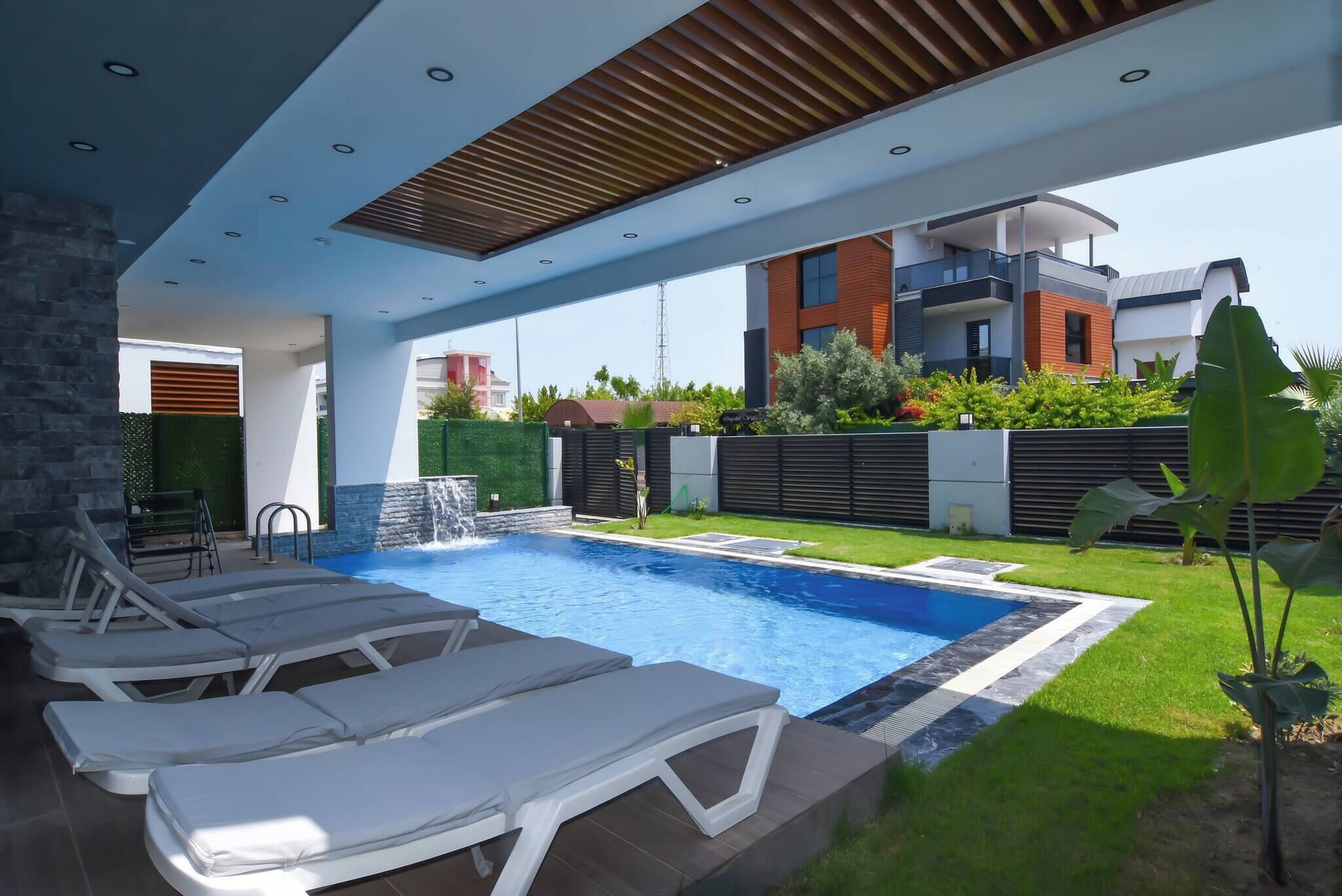 Uma área moderna de piscina ao ar livre com espreguiçadeiras, um muro de pedra e um gramado bem cuidado.