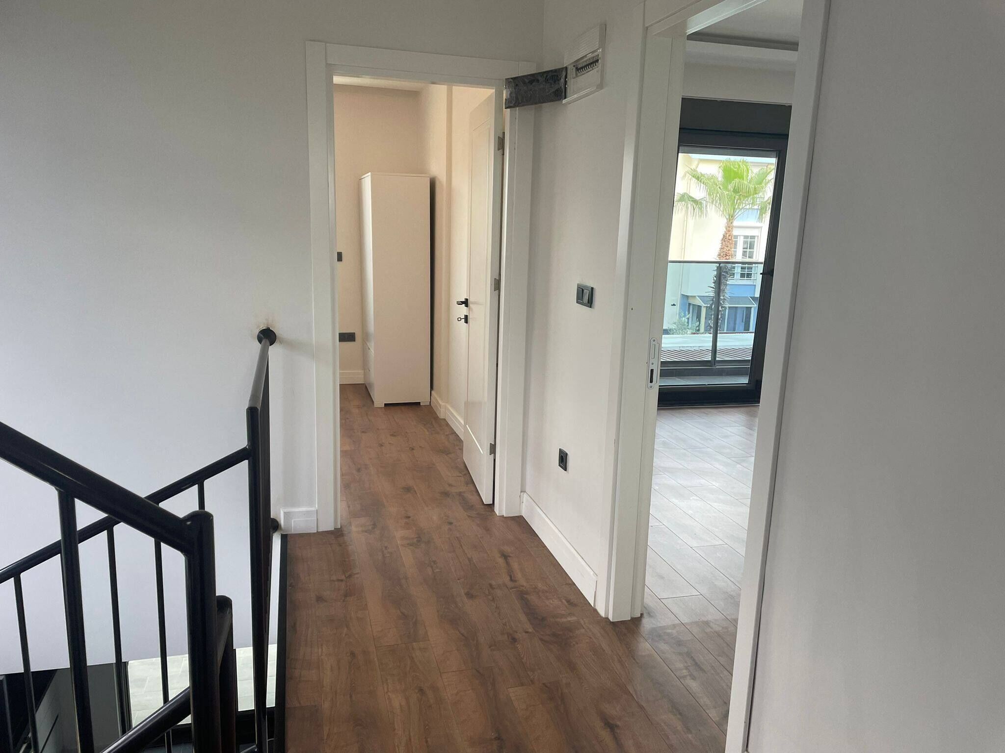 Um corredor com piso de madeira, paredes brancas e corrimão preto.