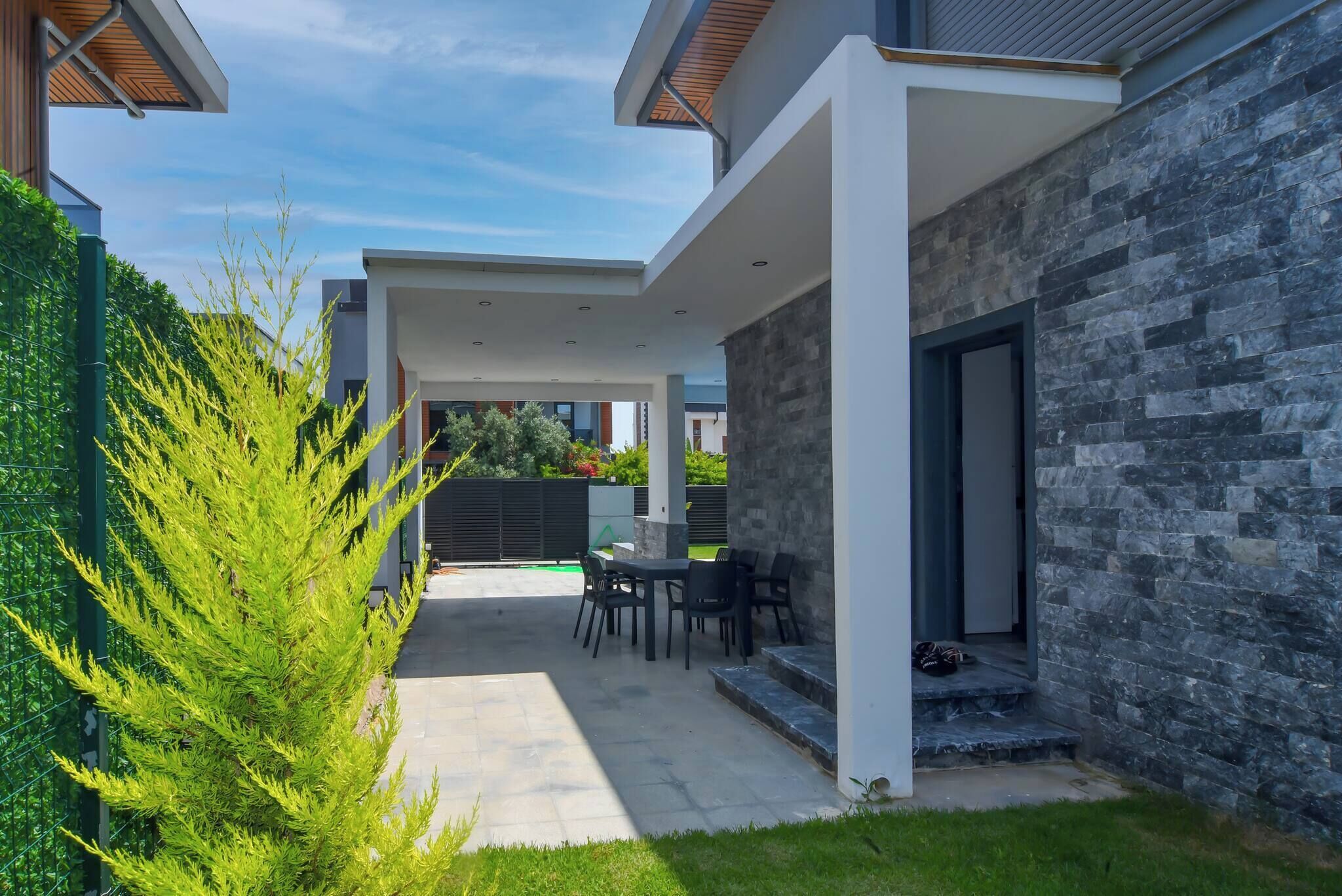 Uma área de terraço moderna ao ar livre, com parede de pedra, espaço para sentar e vista para a paisagem circundante.