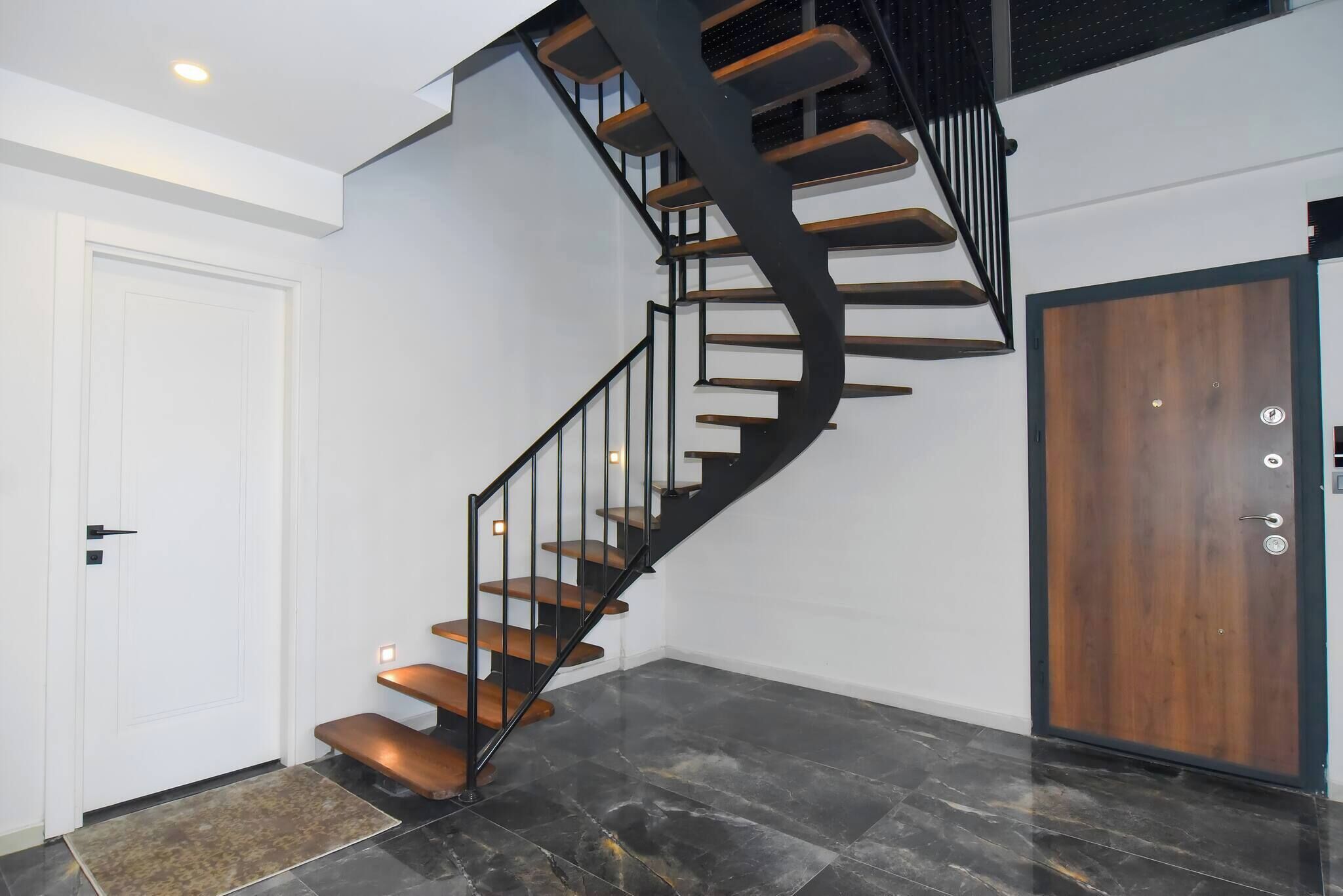 Um interior moderno com uma escada em espiral, uma porta branca e uma porta de madeira.