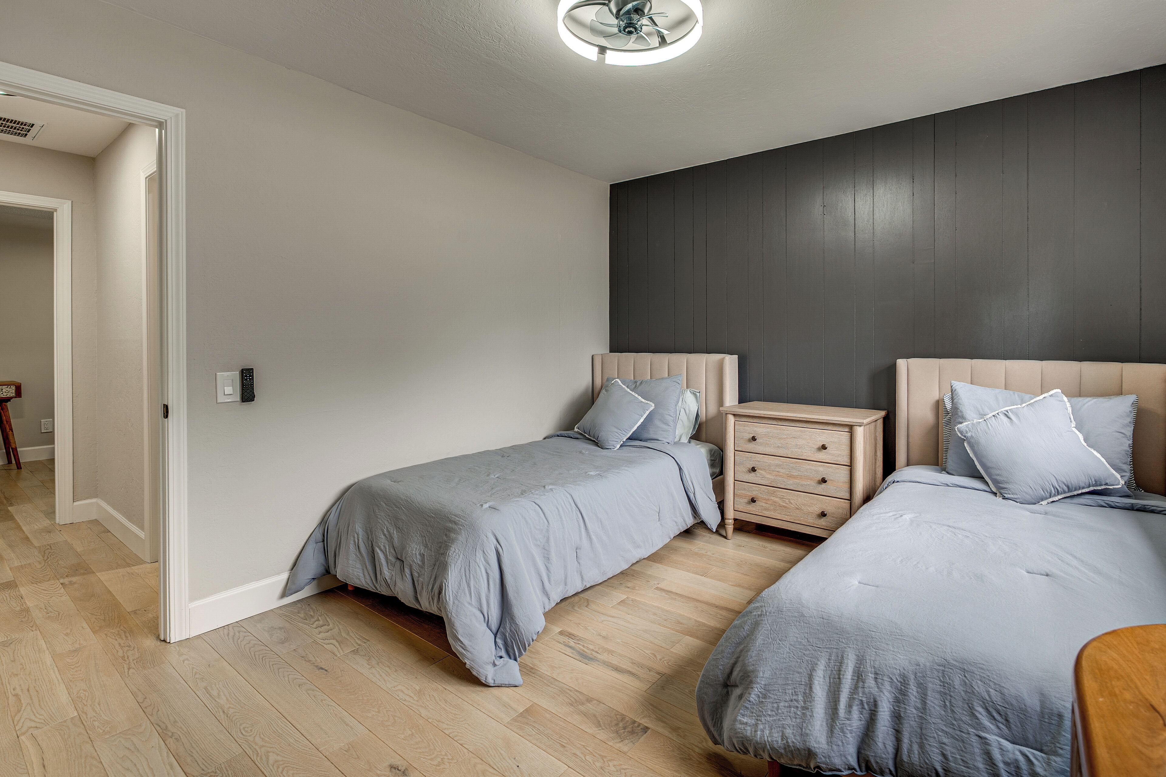 Quarto com duas camas, mesa de cabeceira, guarda-roupa e ventoinha no teto.
