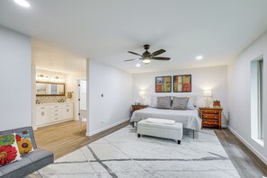 Um quarto com cama, mesas de cabeceira, ventoinha no teto, penteadeira, cômoda, tapete e banheiro com lavatório e espelho.