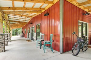 Uma área externa coberta com um edifício vermelho, duas cadeiras, uma mesa e uma bicicleta.